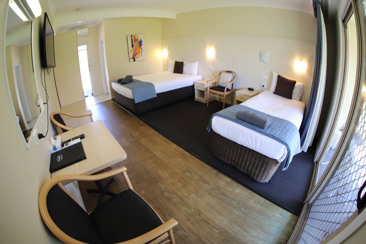 Quarto de hotel pequeno com duas camas de solteiro, uma escrivaninha com cadeira, uma televisão e uma mesinha.