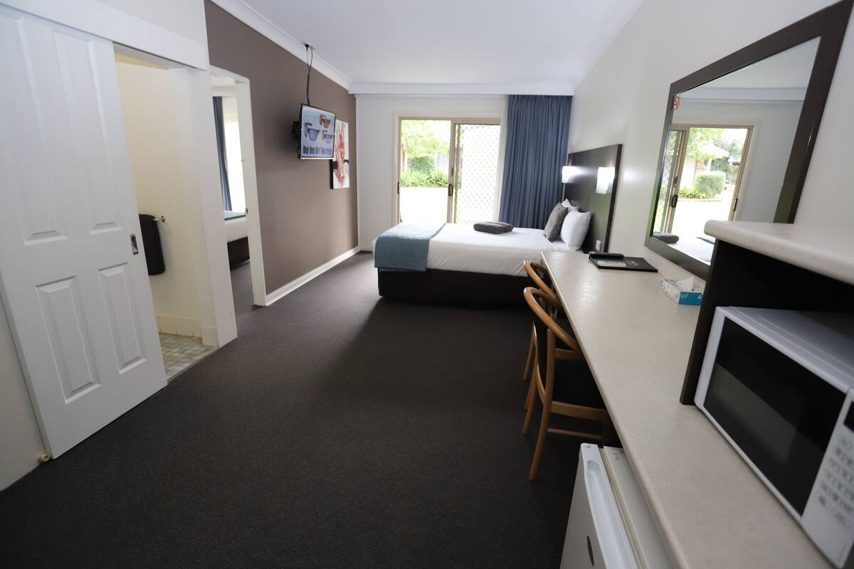Quarto de hotel com uma cama, uma escrivaninha, micro-ondas, televisão e porta para um banheiro.