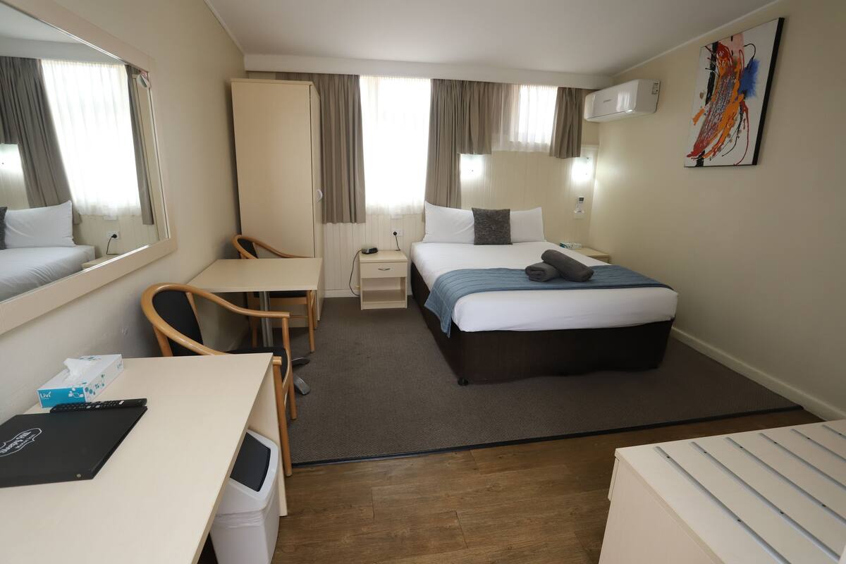 Quarto de hotel com cama, escrivaninha, cadeira e um espelho grande.