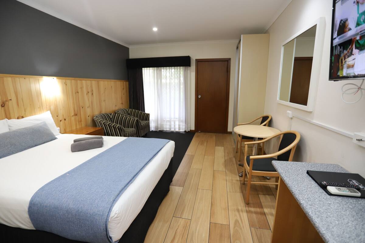 Quarto de hotel com cama, escrivaninha, cadeira, televisão e janela com cortinas.