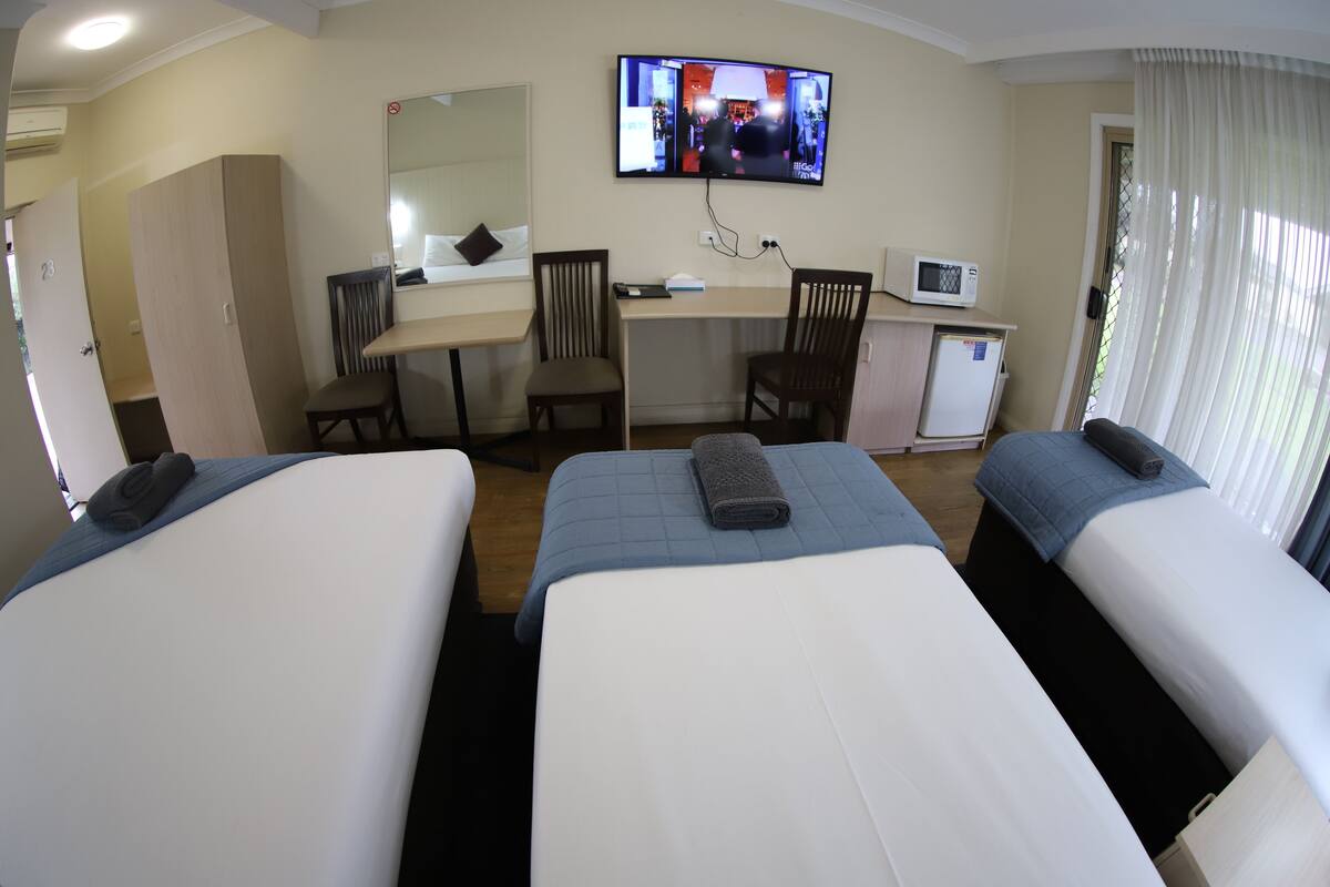 Quarto de hotel com duas camas, uma escrivaninha, uma cadeira, uma televisão e uma kitchenette.