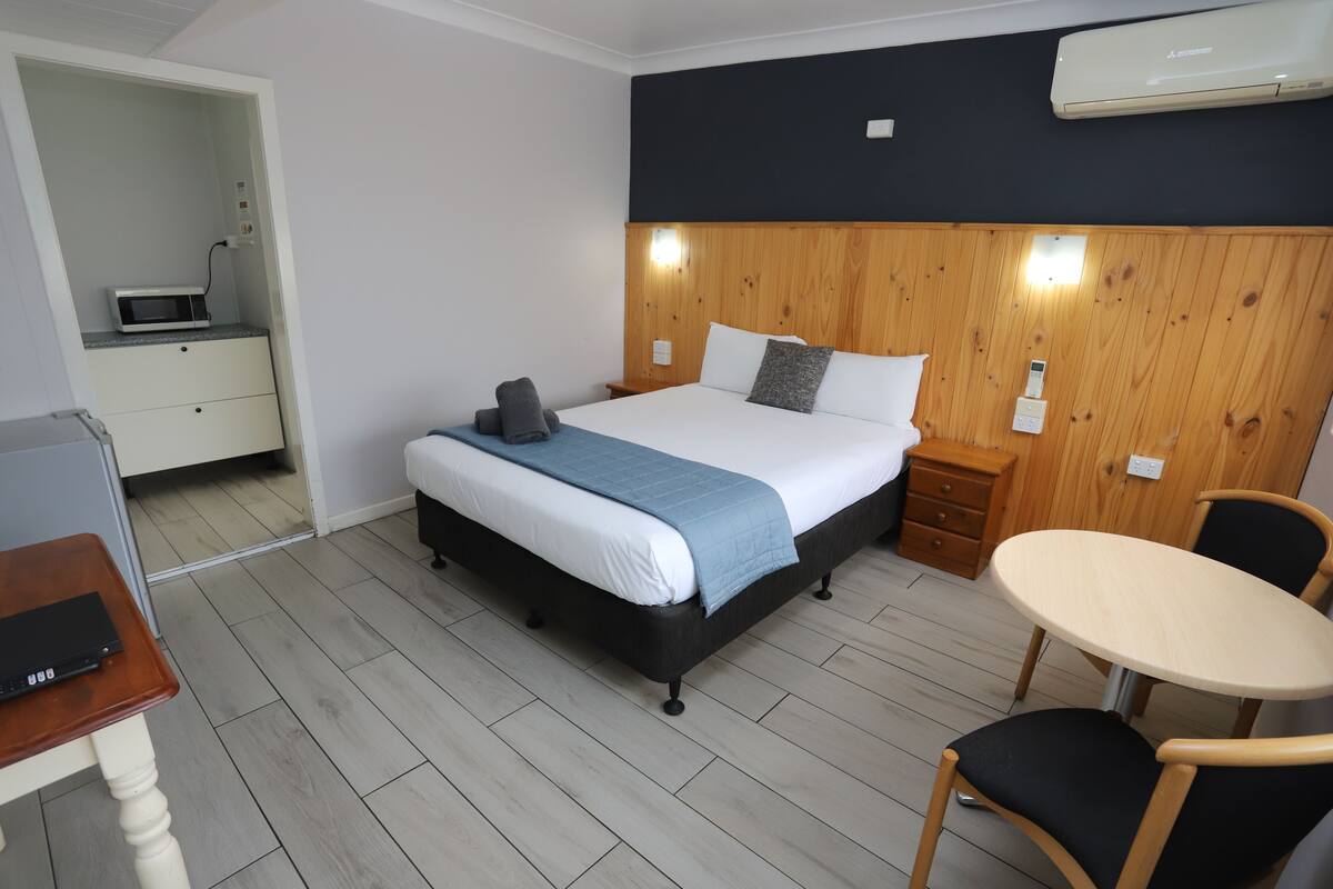 Quarto com cama, mesas de cabeceira, escrivaninha e uma cadeira.