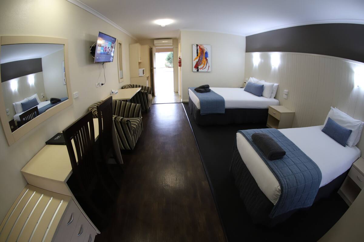 Quarto de hotel com duas camas, uma escrivaninha, uma cadeira, uma televisão e um espelho grande.
