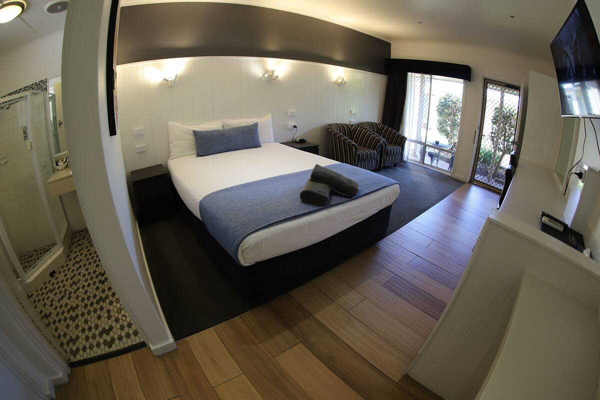 Quarto de hotel moderno com uma cama grande, área de estar com uma poltrona, televisão e porta de vidro deslizante para o exterior.