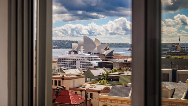 Vista da Casa de Ópera de Sydney e edifícios circundantes através de uma janela.