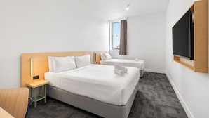 Quarto de hotel moderno com uma cama grande, uma cama menor, uma escrivaninha e uma TV fixada na parede.
