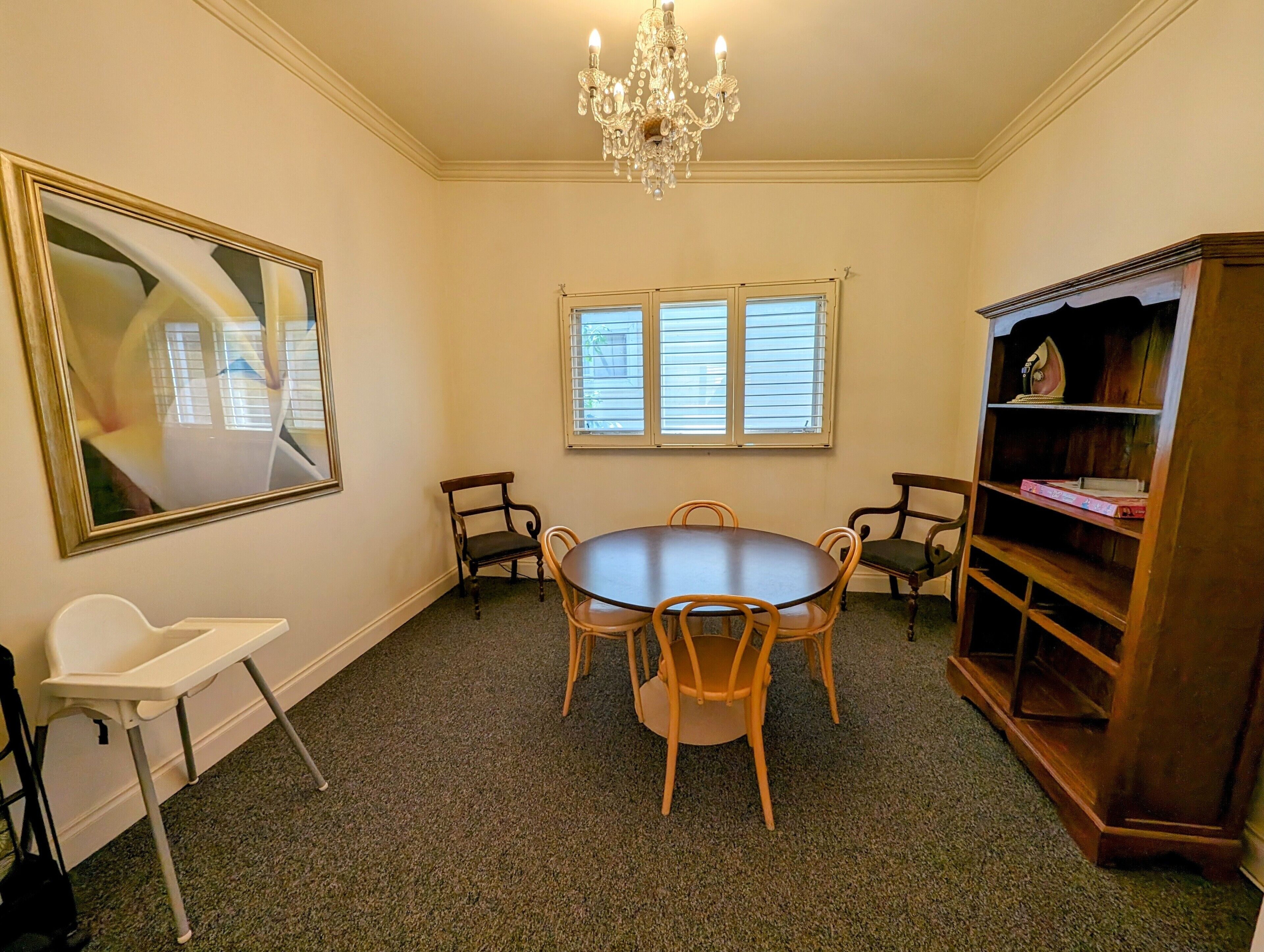 Um quarto com uma mesa redonda, quatro cadeiras, uma estante, um espelho e um candelabro.