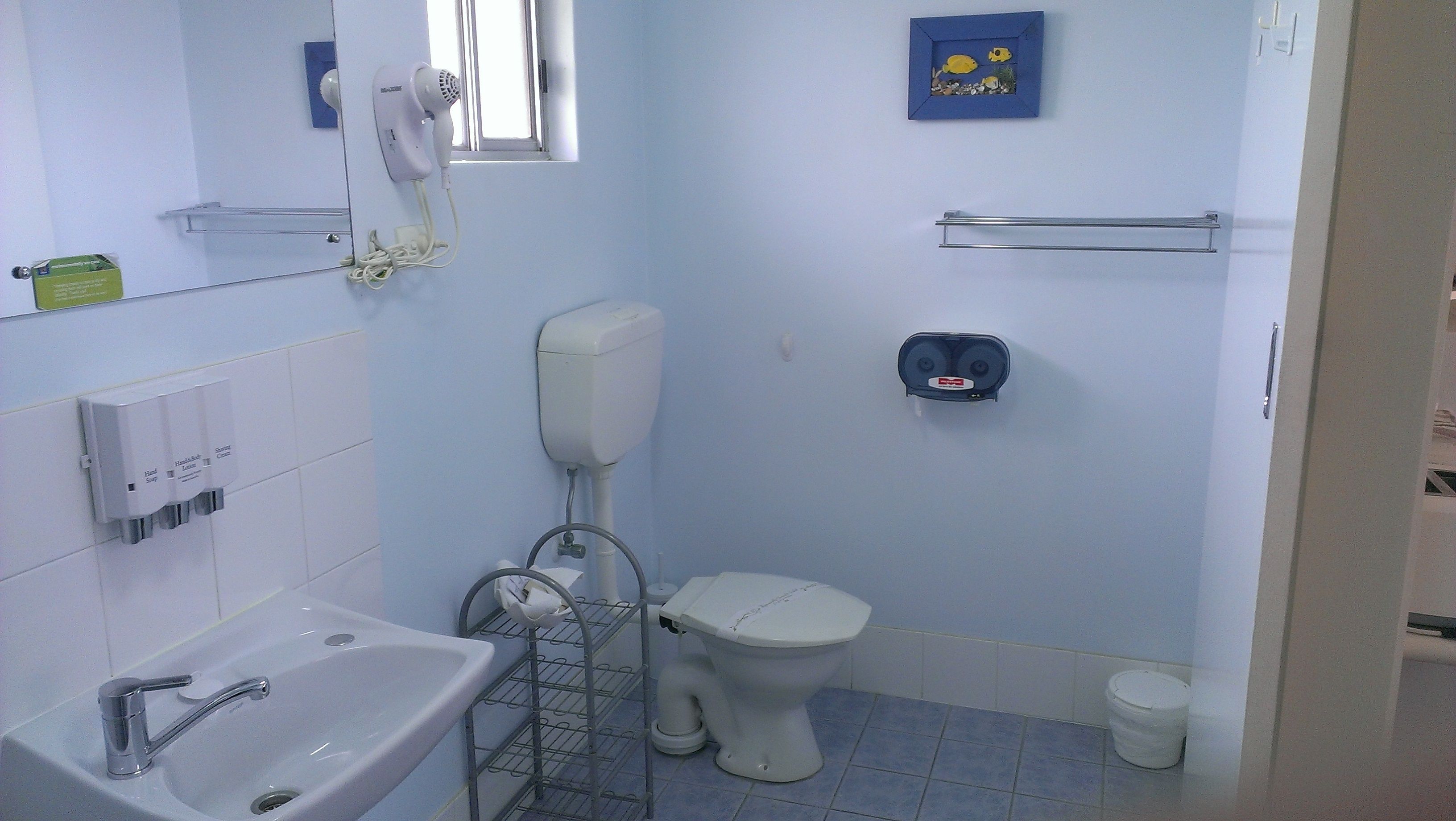 Casa de banho com lavatório branco, sanita, secador de mãos e dispensador de sabão.