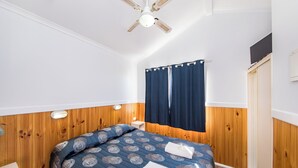 Quarto com cabeceira de madeira, cama com colcha estampada, ventilador de teto e janela com cortinas.