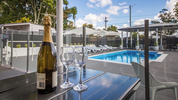 Uma área à beira da piscina com uma mesa, uma garrafa de champanhe e duas taças.