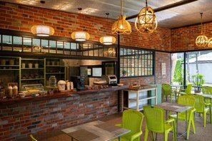 Café com paredes de tijolos, balcão, área de estar e luminárias pendentes.