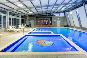 Piscina interna com várias pistas, cadeiras de descanso e um grande mural em formato de coração na parede.