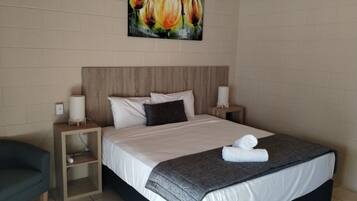Quarto de hotel com uma cama, duas mesas de cabeceira, um criado-mudo, um quadro na parede e uma cadeira.