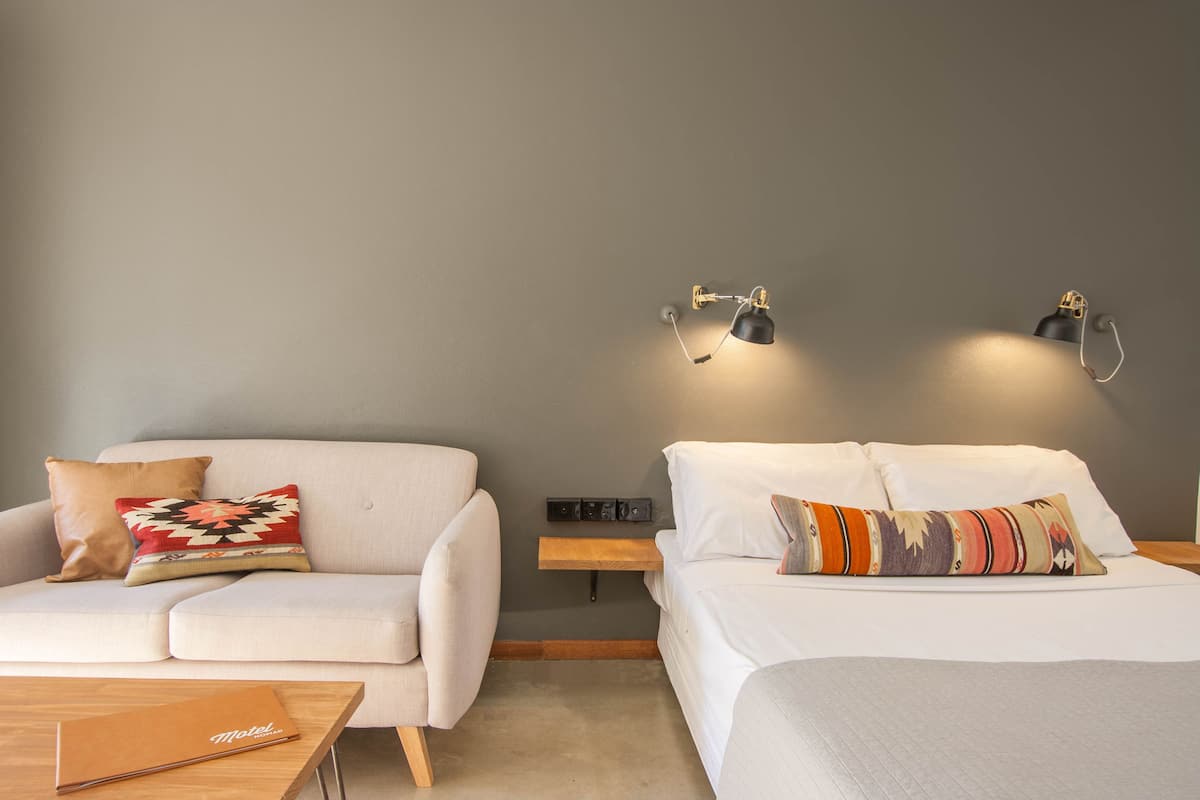 Quarto moderno com sofá, cama, mesa de cabeceira e luminária fixada na parede.