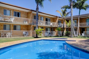 Um hotel com vários andares, piscina, área de estar externa e palmeiras.