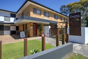 Um edifício moderno de apartamentos com dois andares, com uma porta vermelha, uma placa de identificação e entrada com portão.