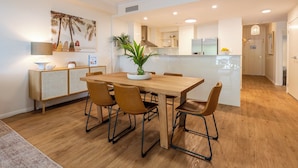 Cozinha moderna com armários brancos, uma ilha central e um espaço de jantar com mesa e cadeiras de madeira.