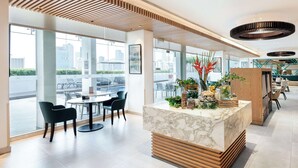 Um hall de hotel moderno com uma recepção de mármore, cadeiras pretas e vista para a cidade através de grandes janelas.