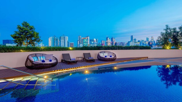 Piscina no terraço com espreguiçadeiras e vista para o horizonte da cidade.