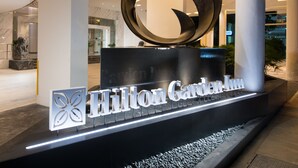 A entrada do Hilton Garden Inn, com uma grande escultura circular e o nome do hotel em destaque.