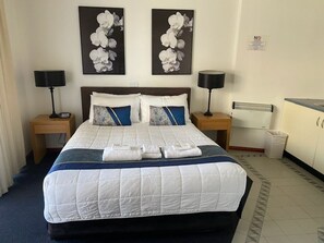 Quarto de hotel com uma cama grande, duas mesas de cabeceira, uma escrivaninha e uma lixeira.