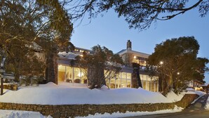 Um hotel com fachada de pedra, grandes janelas e arredores cobertos de neve.