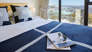 Quarto de hotel com uma cama grande, vista para as montanhas e varanda com grade.