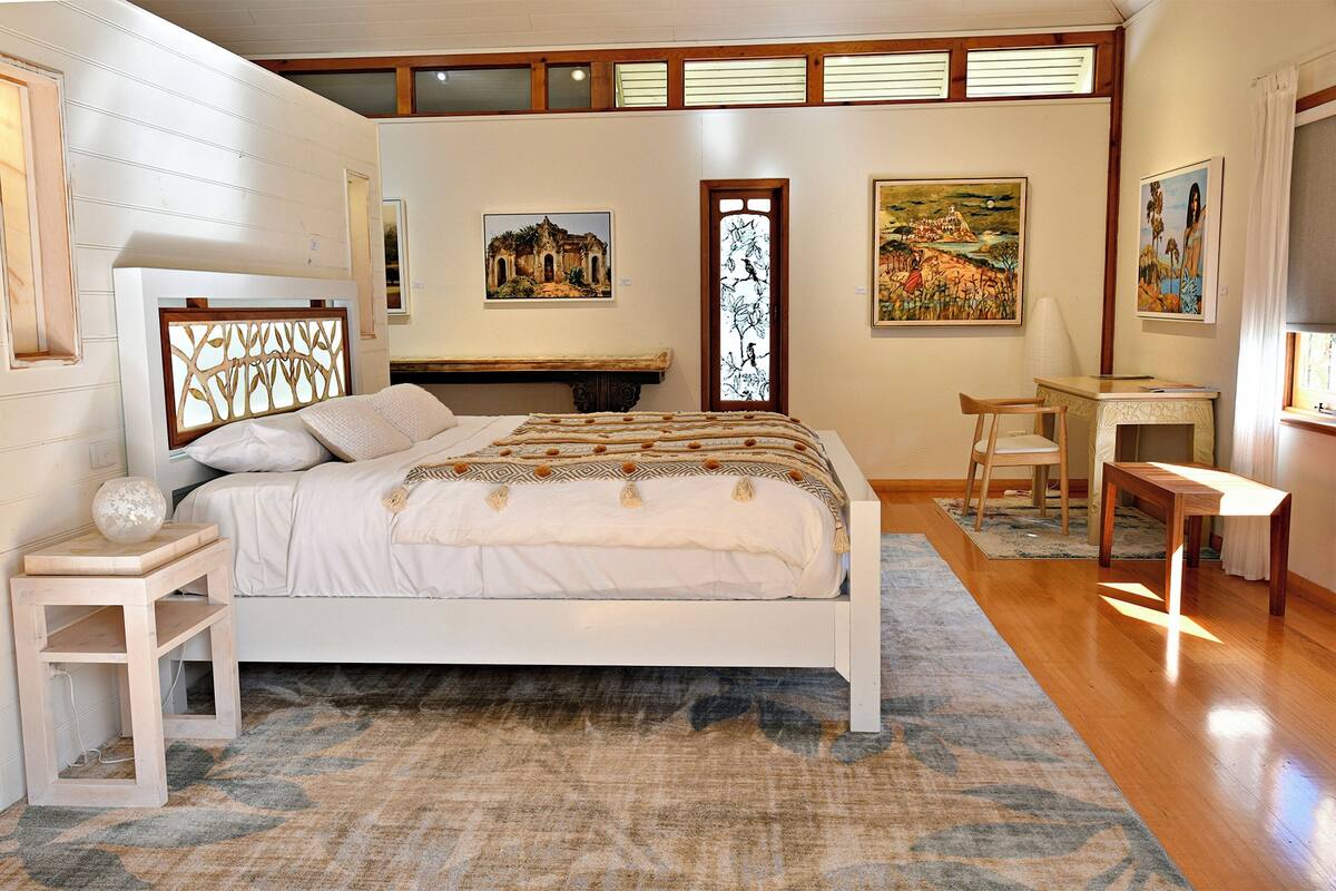 Quarto com cama, mesas de cabeceira, escrivaninha e obras de arte nas paredes.