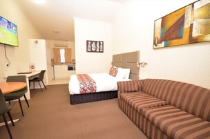 Quarto de hotel com cama, sofá, escrivaninha e televisão.