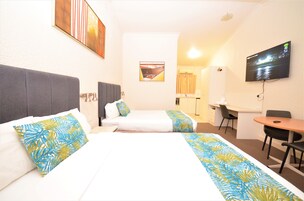 Quarto de hotel com duas camas, uma escrivaninha, uma cadeira, televisão e obras de arte nas paredes.
