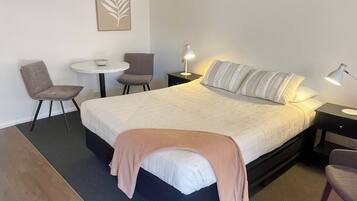 Quarto de hotel moderno com uma cama grande, uma pequena escrivaninha, duas cadeiras, uma mesa redonda e um ar condicionado fixado na parede.