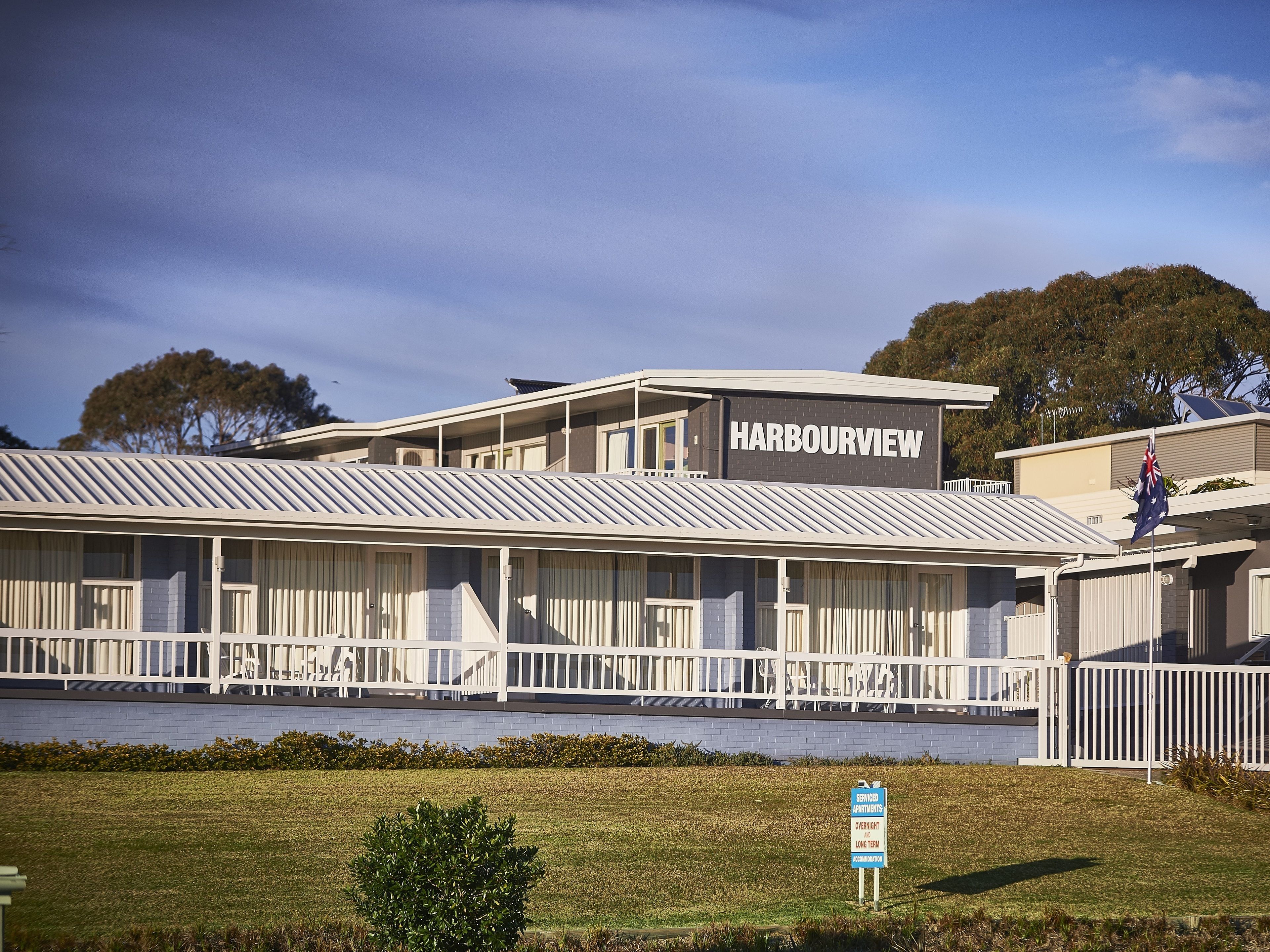 Um edifício com uma placa com a inscrição 'Harbourview' e outra placa indicando 'Alojamento de apartamentos com serviços para pernoite'.