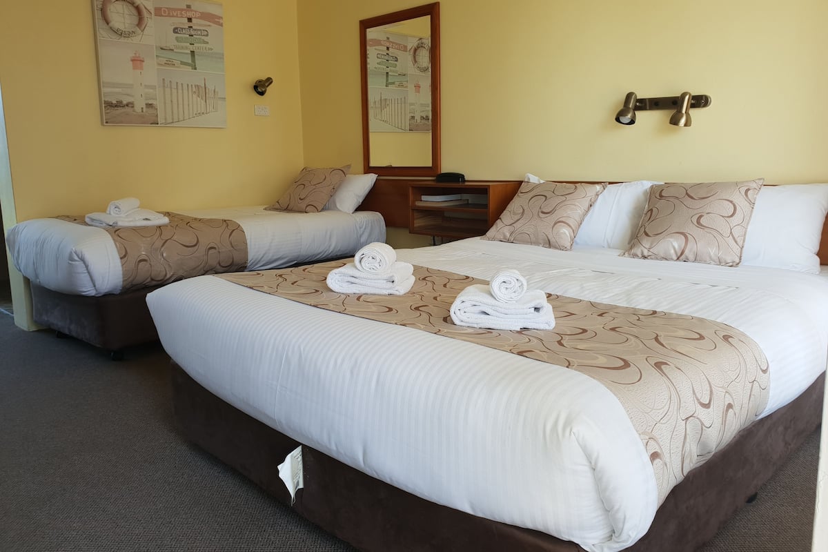 Quarto de hotel com duas camas de solteiro e uma cama de casal, cada uma com toalhas bem dobradas.