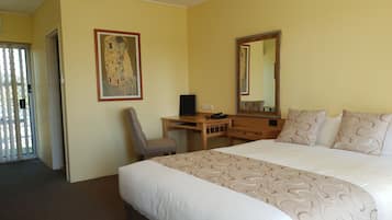 Quarto de hotel com uma cama grande, uma escrivaninha com cadeira, luminária de mesa, telefone, quadro emoldurado e um espelho.