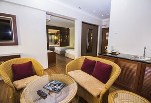 Quarto de hotel com mobiliário de vime, mesa de centro de vidro, cama e cozinha compacta.