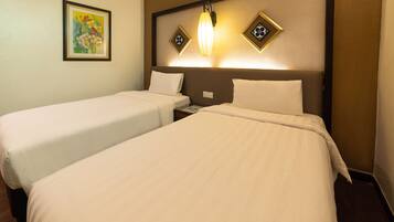 Quarto de hotel com duas camas de solteiro, mesa de cabeceira, telefone e luminária fixa na parede.