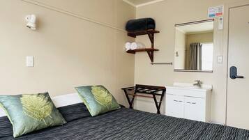 Quarto de hotel com cama, uma pequena escrivaninha, espelho e prateleira com toalhas.