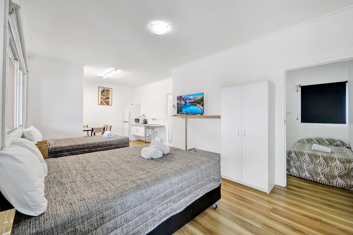 Quarto de hotel moderno com uma cama grande, uma escrivaninha, uma televisão e um guarda-roupa.