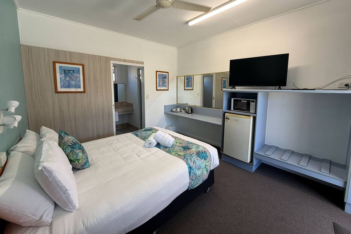 Quarto de hotel com cama, televisão, micro-ondas, chuveiro e banheiro.