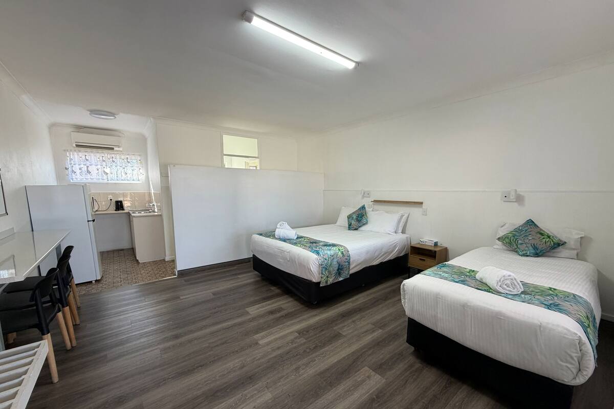 Quarto de hotel com duas camas, uma kitchenette pequena e uma escrivaninha.