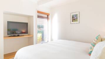 Quarto com cama, televisão em uma estante, janela com persianas e quadro na parede.