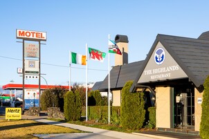 Um motel e um restaurante, com bandeiras, uma placa de identificação e um letreiro de aluguel de carros.