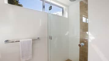 Um chuveiro moderno com porta de vidro, porta-toalhas e vista do céu pela janela.