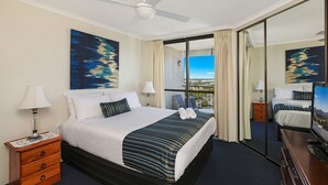 Quarto de hotel com cama, mesa de cabeceira, cômoda, ventoinha no teto e uma grande janela com vista.