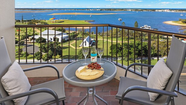 Varanda com mesa posta para dois, vista para uma marina com barcos e um campo de golfe.