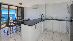 Cozinha moderna com armários brancos, bancada preta e vista para o mar através de uma porta de correr de vidro.