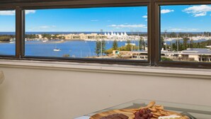 Mesa com tábua de queijos e uvas em um quarto com vista para um porto e edifícios.