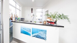Uma área de recepção com balcão, duas fotos aéreas emolduradas, uma planta em vaso e um modelo de navio.