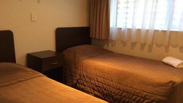 Quarto de hotel com duas camas de solteiro, uma mesa de cabeceira e uma janela com cortinas.