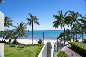 Uma varanda com vista para uma praia, palmeiras e um céu azul límpido.